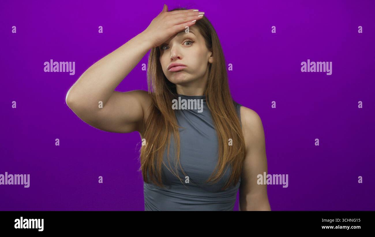 Young woman with hand on forehead and wide eyed expression in a studio ...