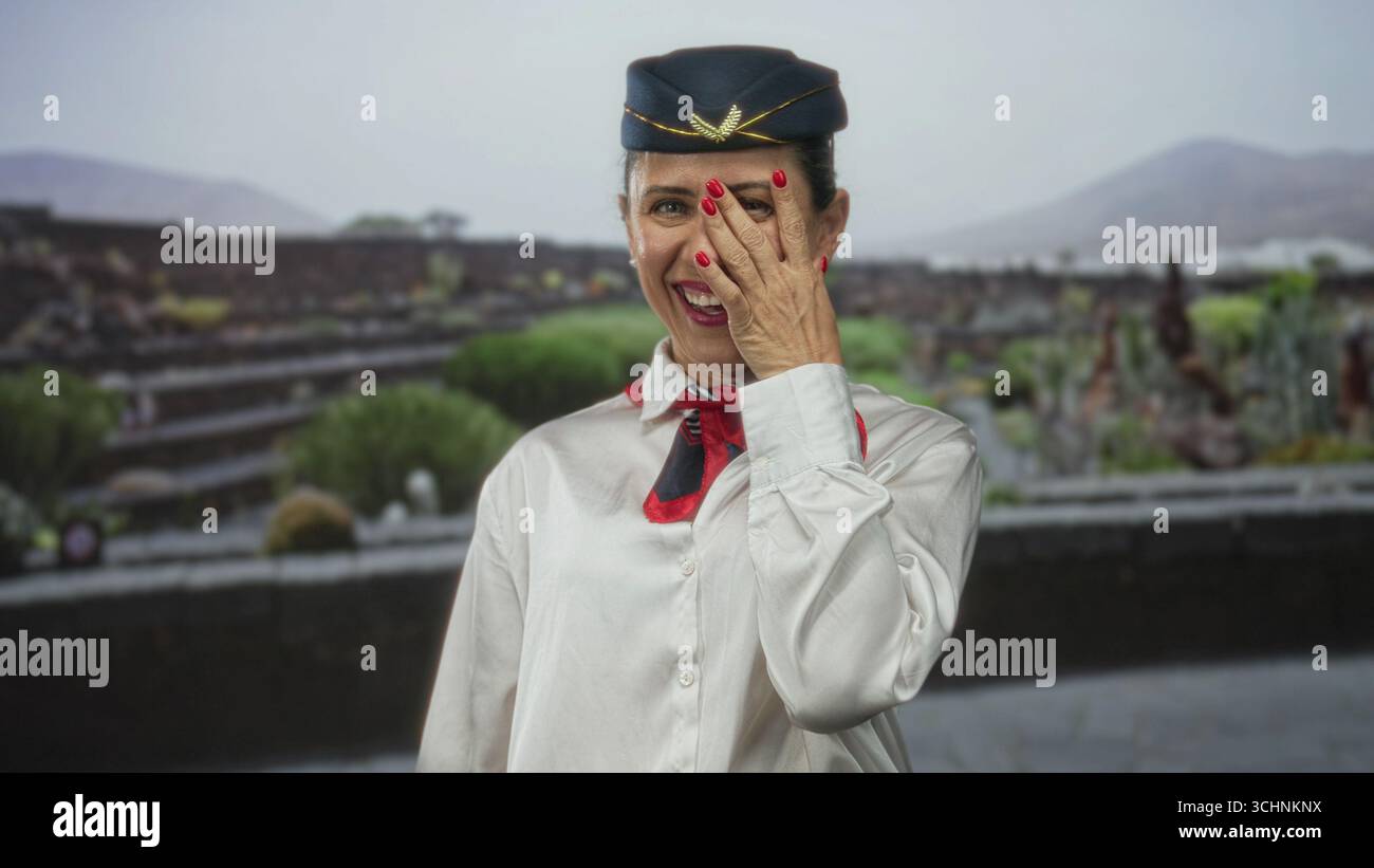 Woman laughing with hand near face wearing airline uniform hat and red ...