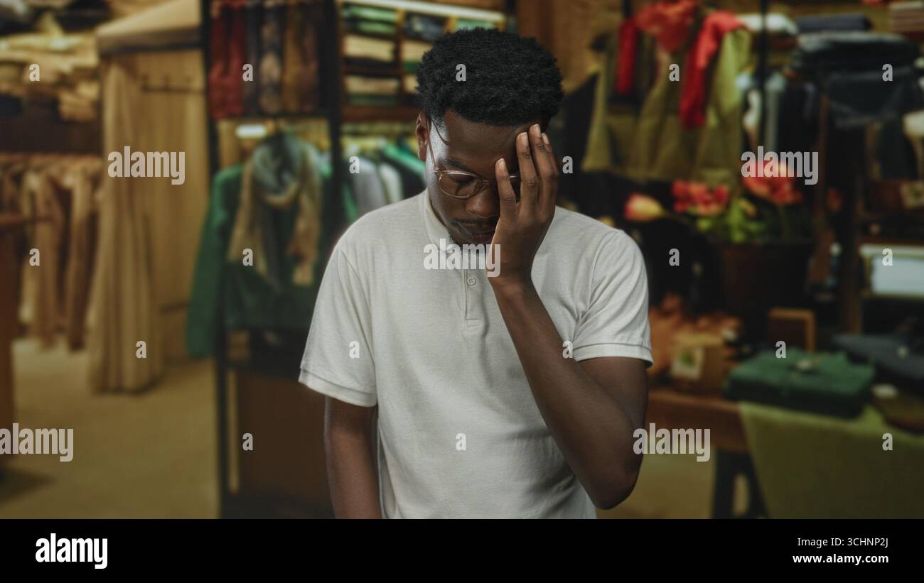 Man holds hand to temple in clothing store as he browses shelves and ...