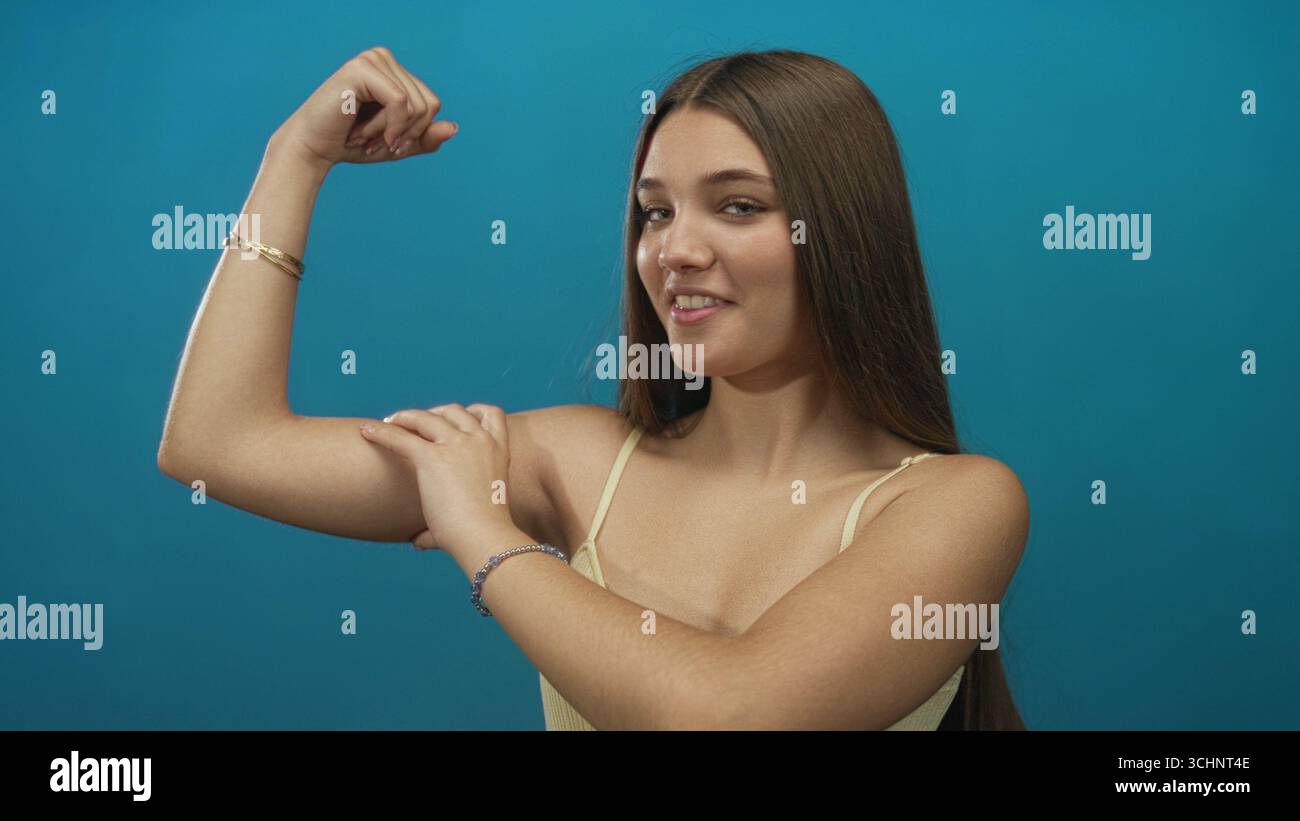 Teen girl wearing beige tank top flexes biceps in bright studio with ...