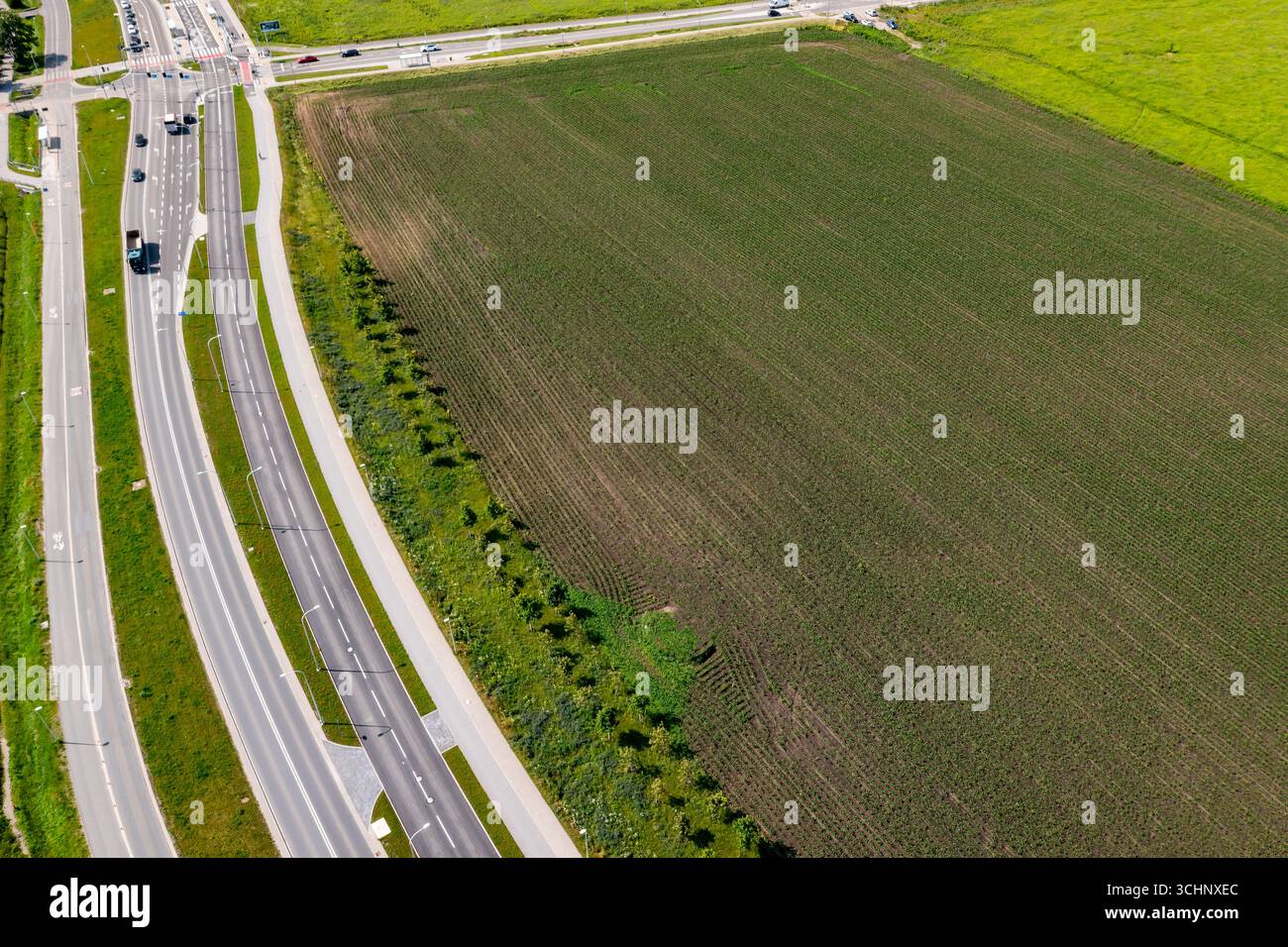 Urban bypass road running along large plowed field and green belt with ...