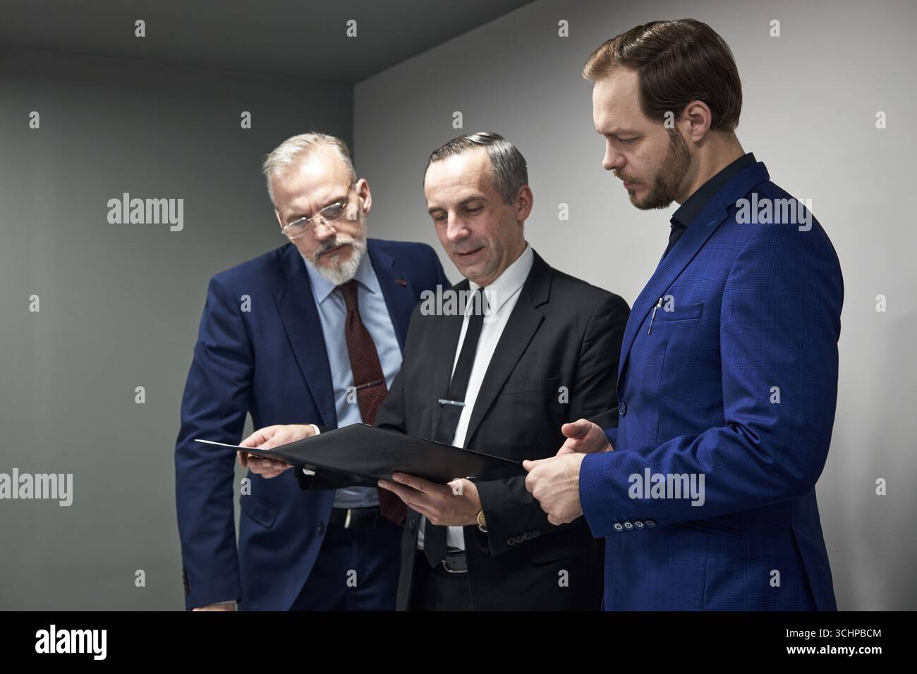 Three middle aged Caucasian men standing together reviewing documents ...