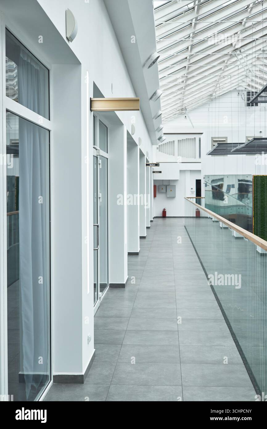 Modern empty corridor featuring glass railing and large windows ...