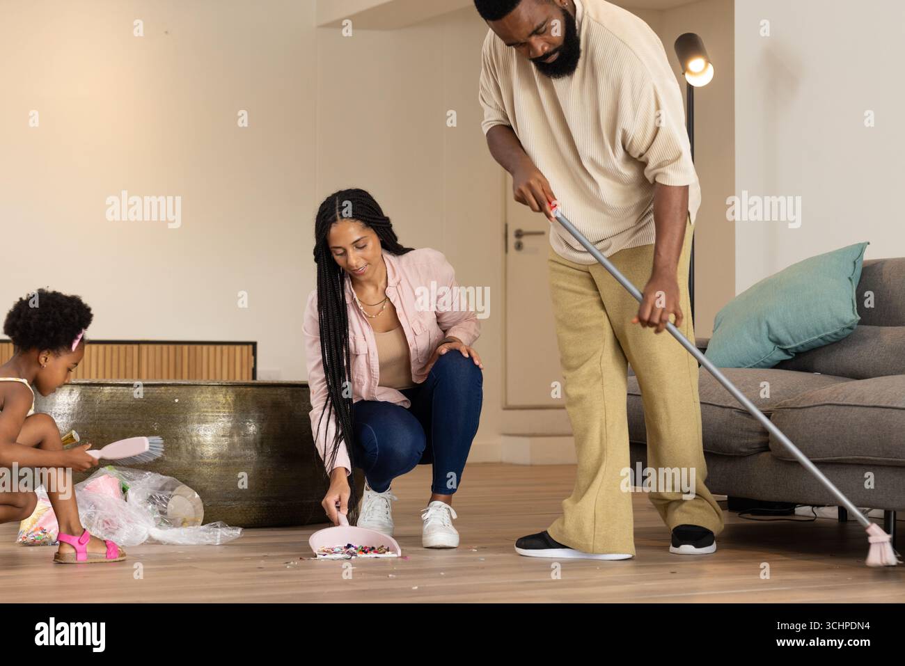 Family cleaning living room together, sweeping and picking up trash ...