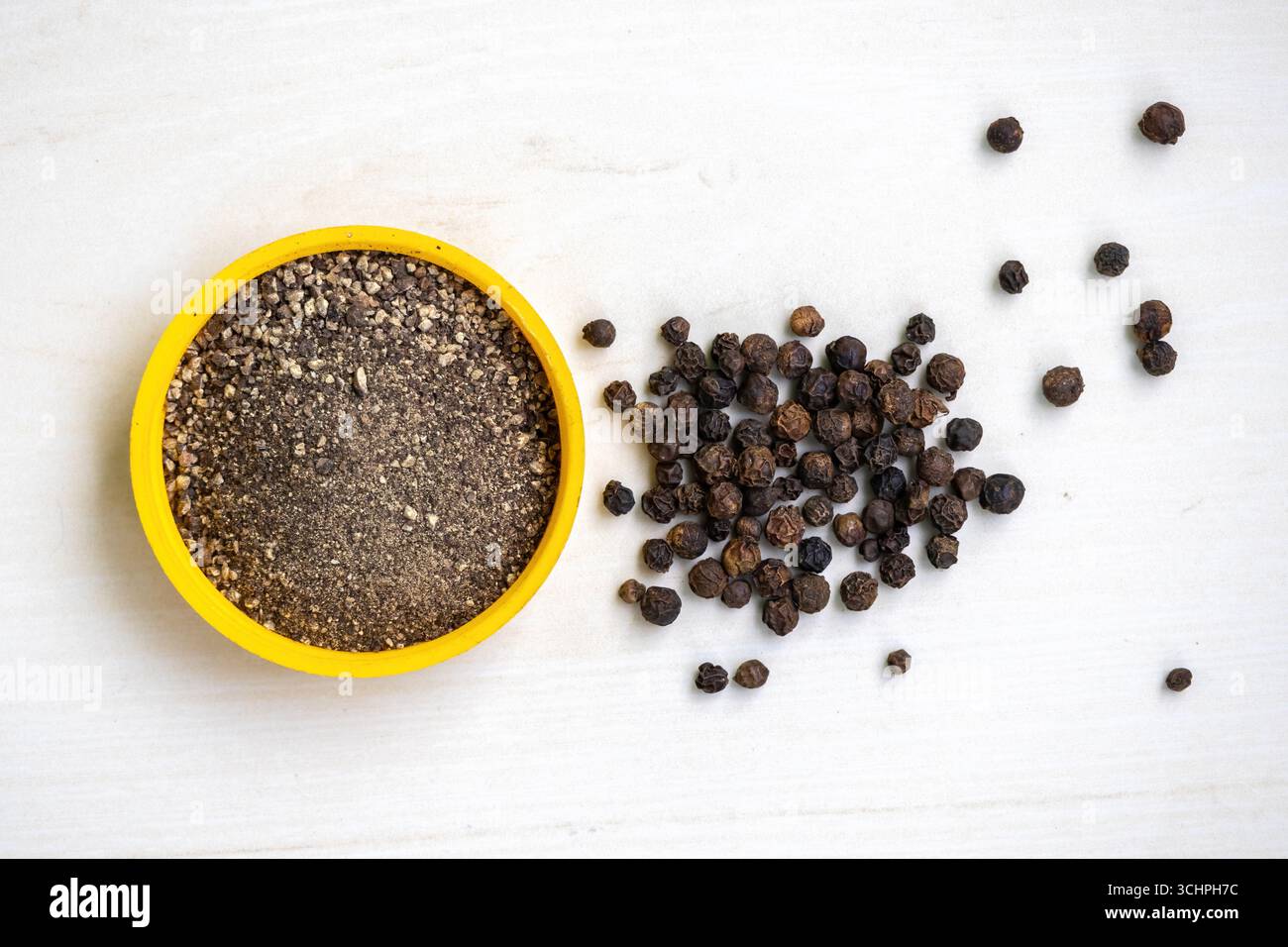 Crushed black pepper in a yellow container and whole black peppers ...