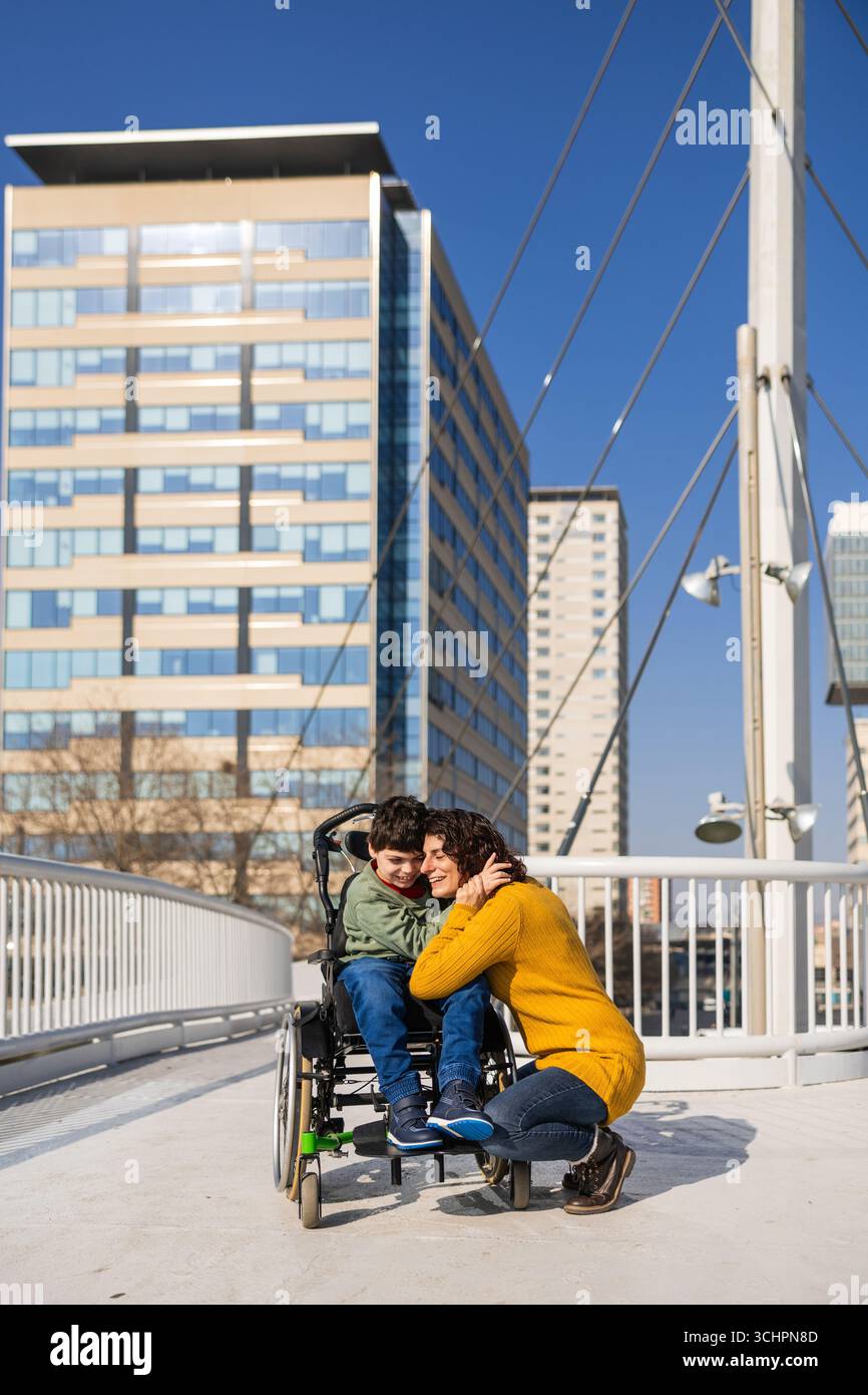 Mother hugging son with disability in wheelchair on bridge Stock Photo ...