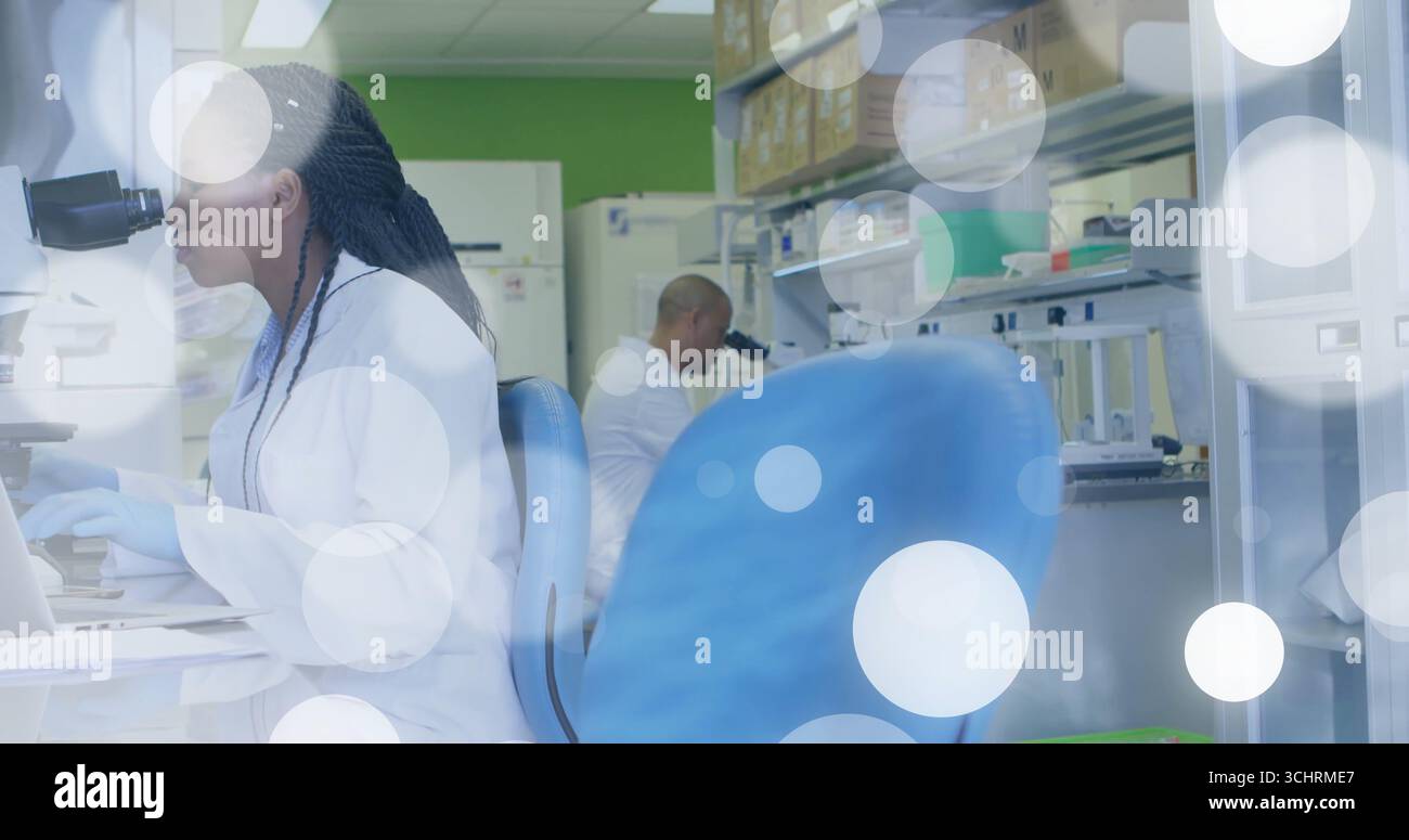 Peering woman technician wearing coat examining sample under microscope ...