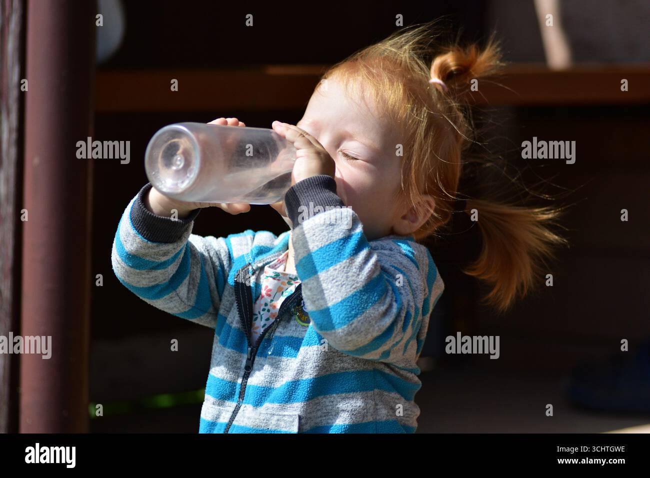 Red-haired toddler girl drinks water from transparent bottle in ...