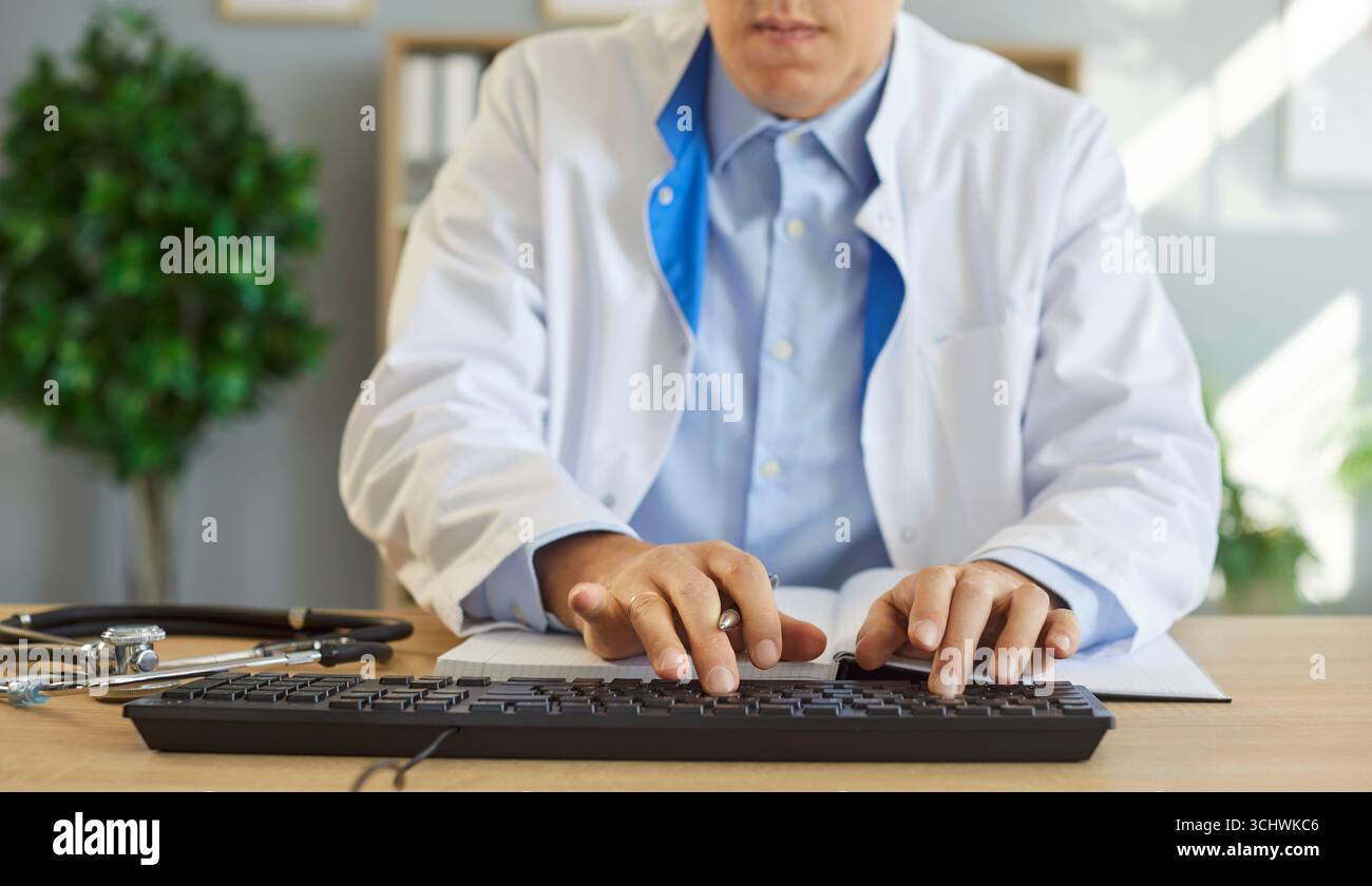Unknown doctor sitting at workplace in his cabinet, typing on keyboard ...