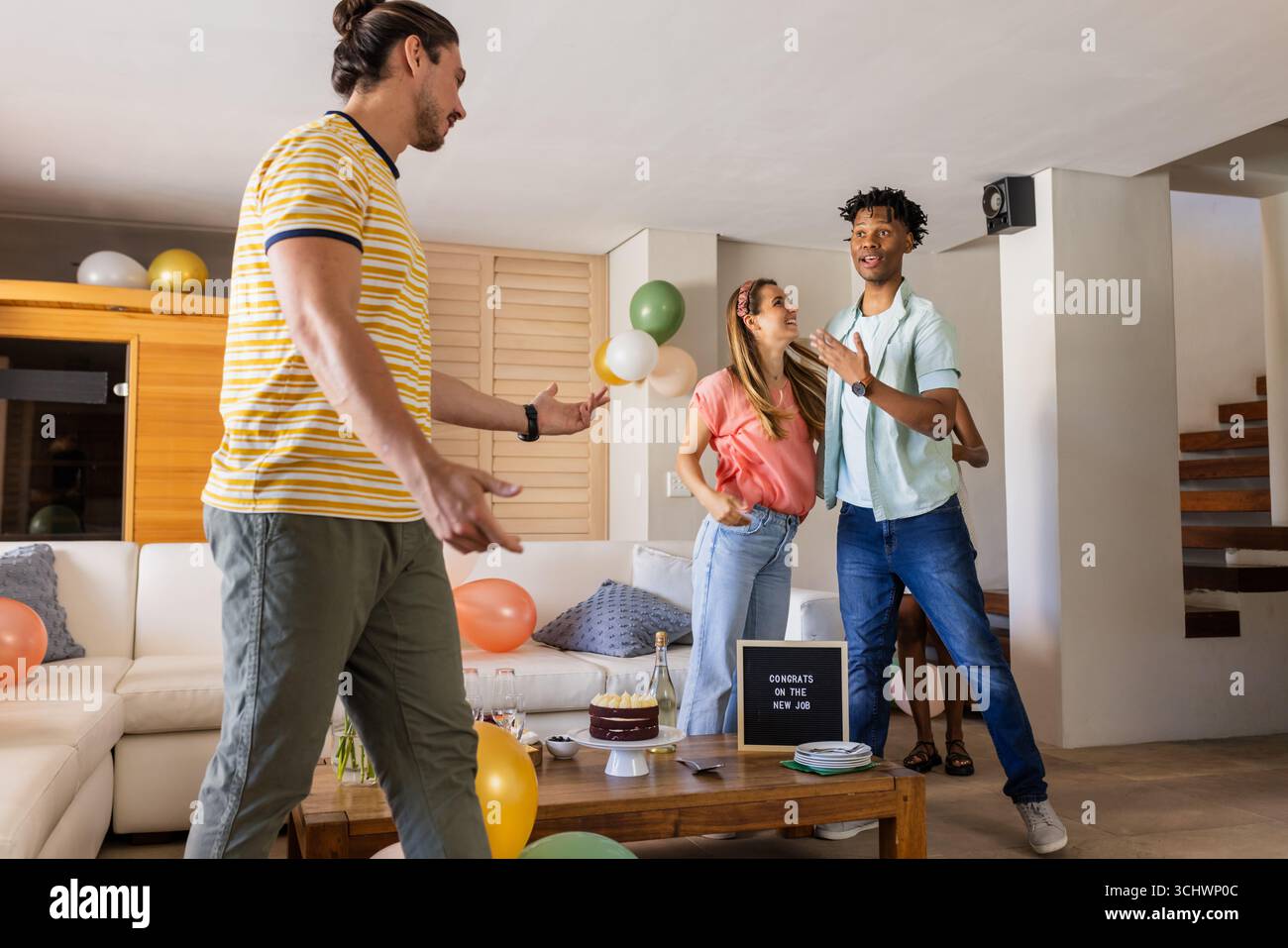 Friends celebrating new job with balloons and cake in living room ...
