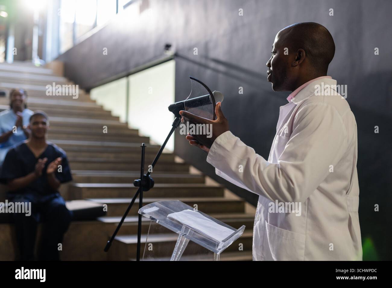 Professional man in white coat presenting award on stage while audience ...