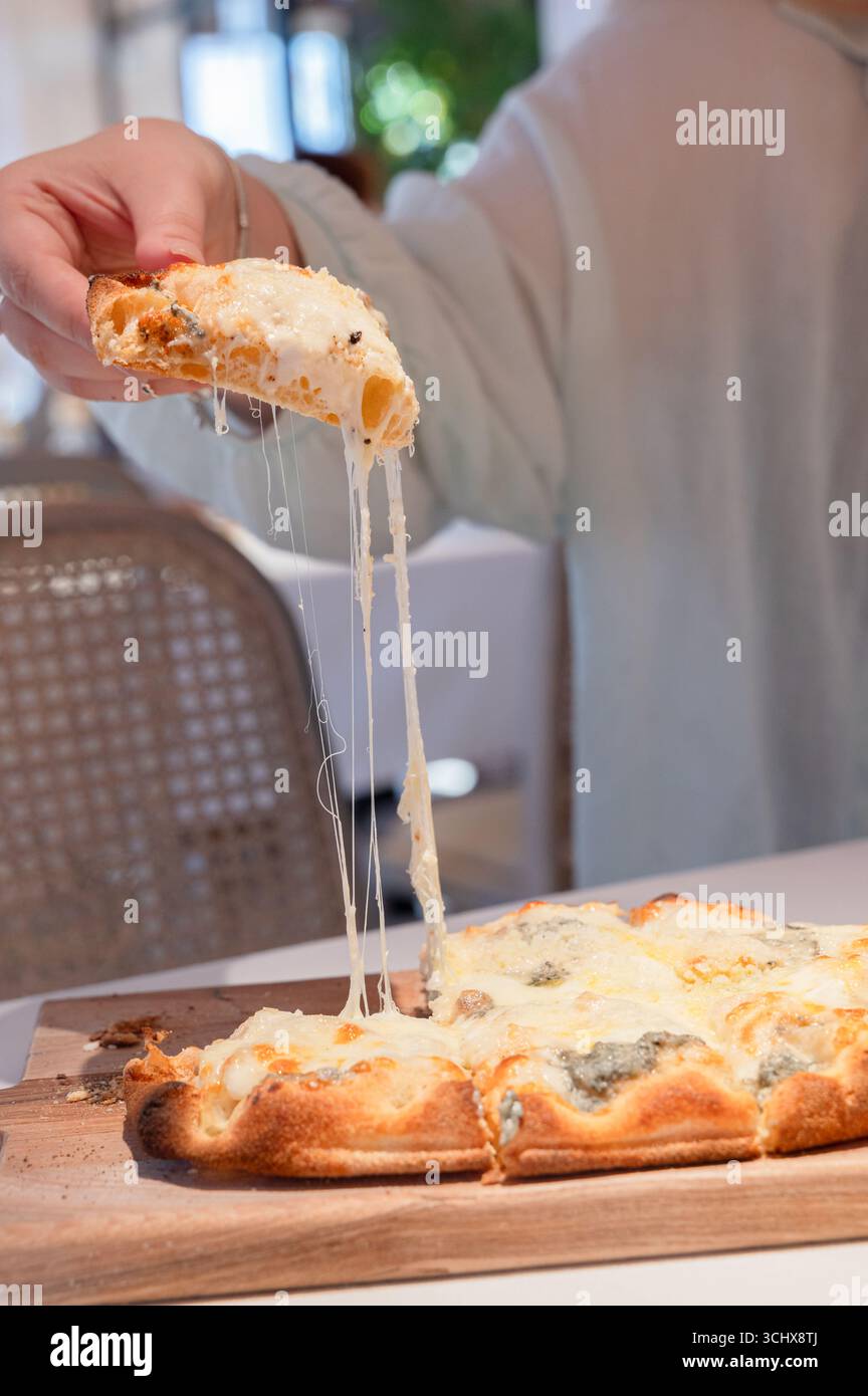 A deliciously tempting slice of cheesy pizza is being pulled apart, showcasing gooey melted ...