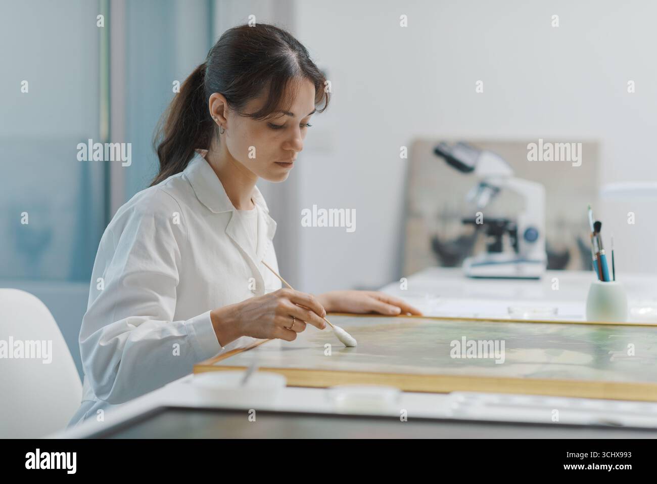 Painting conservator working in the laboratory, she is cleaning an ...