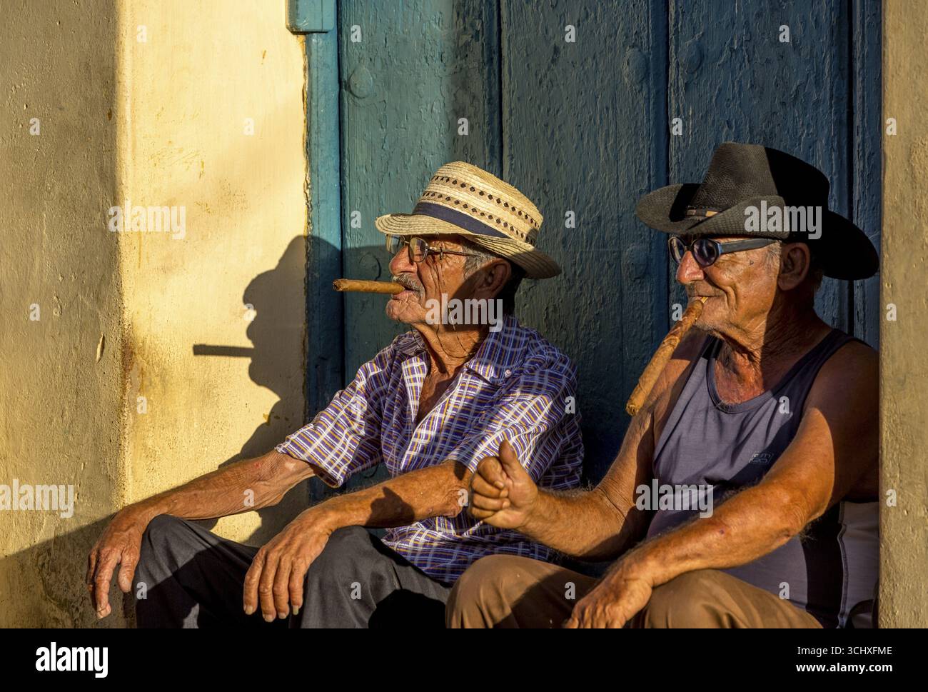 An old Cuban smokes a cigar and sits on a staircase in the warm light ...