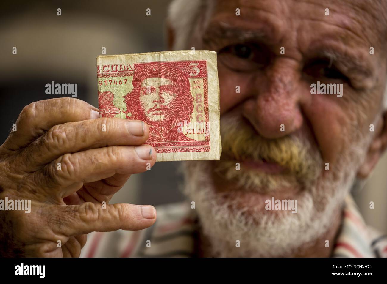 Old Cuban man holding a three peso banknote with the portrait of ...