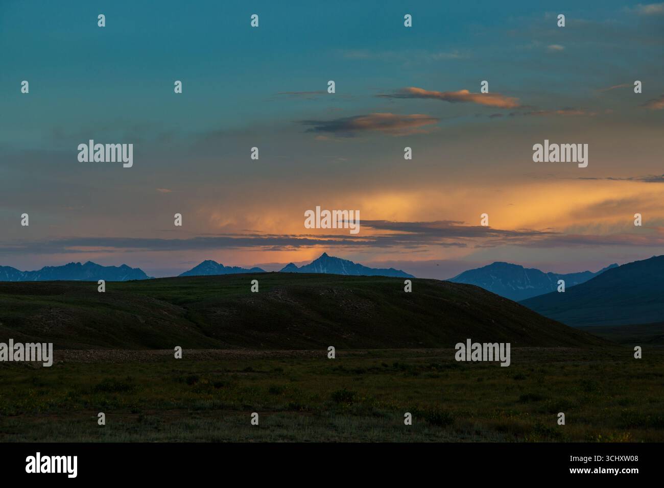 View of green hills rolling under a sky ablaze with sunset hues ...