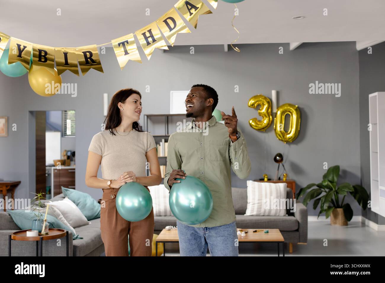 Diverse couple celebrating birthday at home with balloons and festive ...