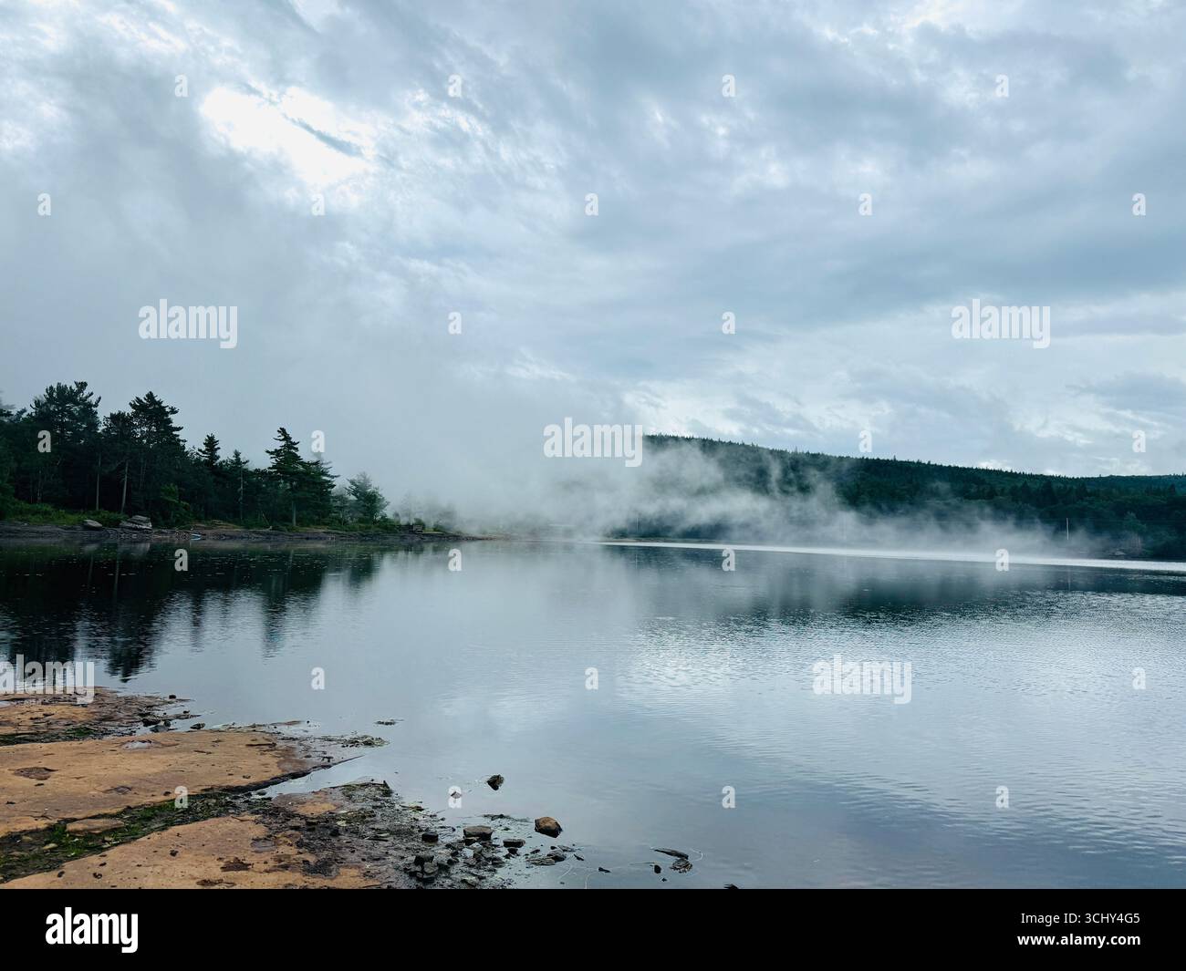 Dense, thick, grey sunrise mist and morning fog rolls in over water at ...