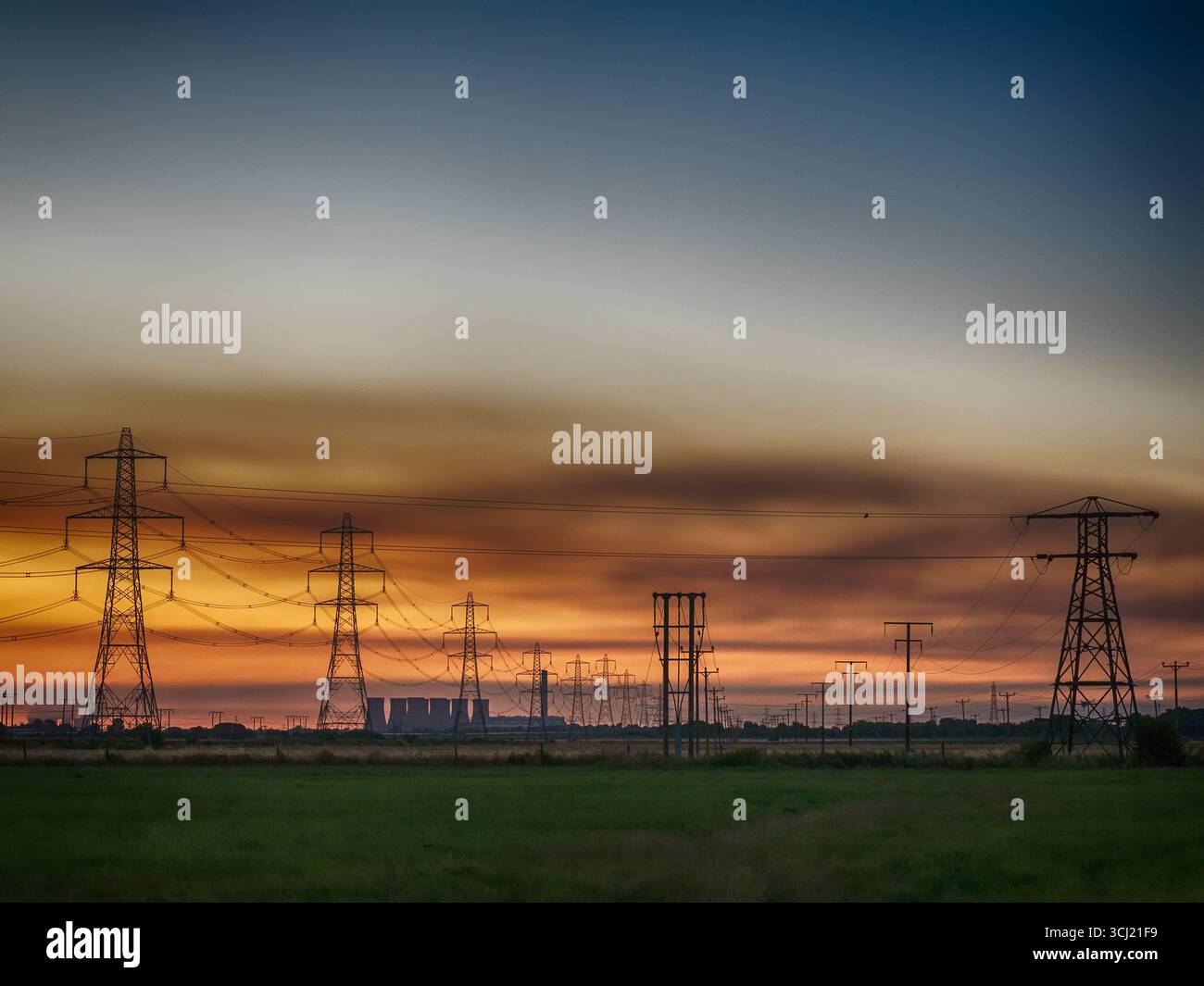 Electricity pylons and power lines at sunrise with cooling towers on ...