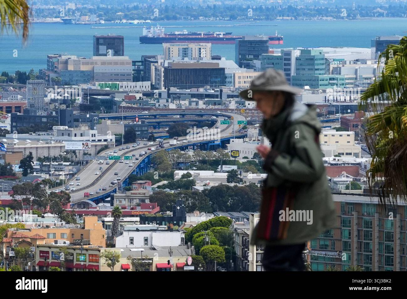 A pedestrian crosses the street in front of a freeway ramp and the bay ...