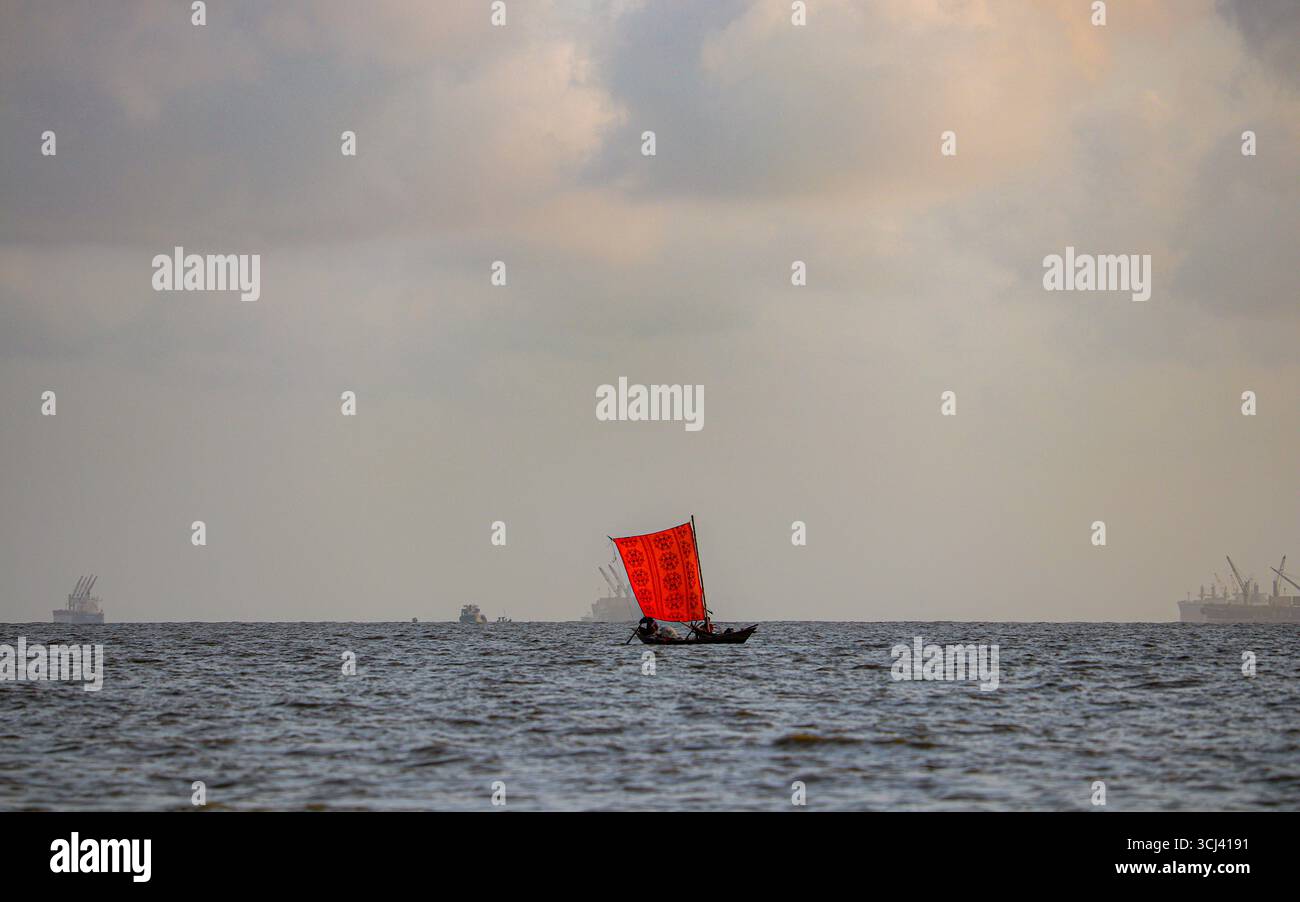 A traditional fishing boat with a striking red sail drifts across the ...