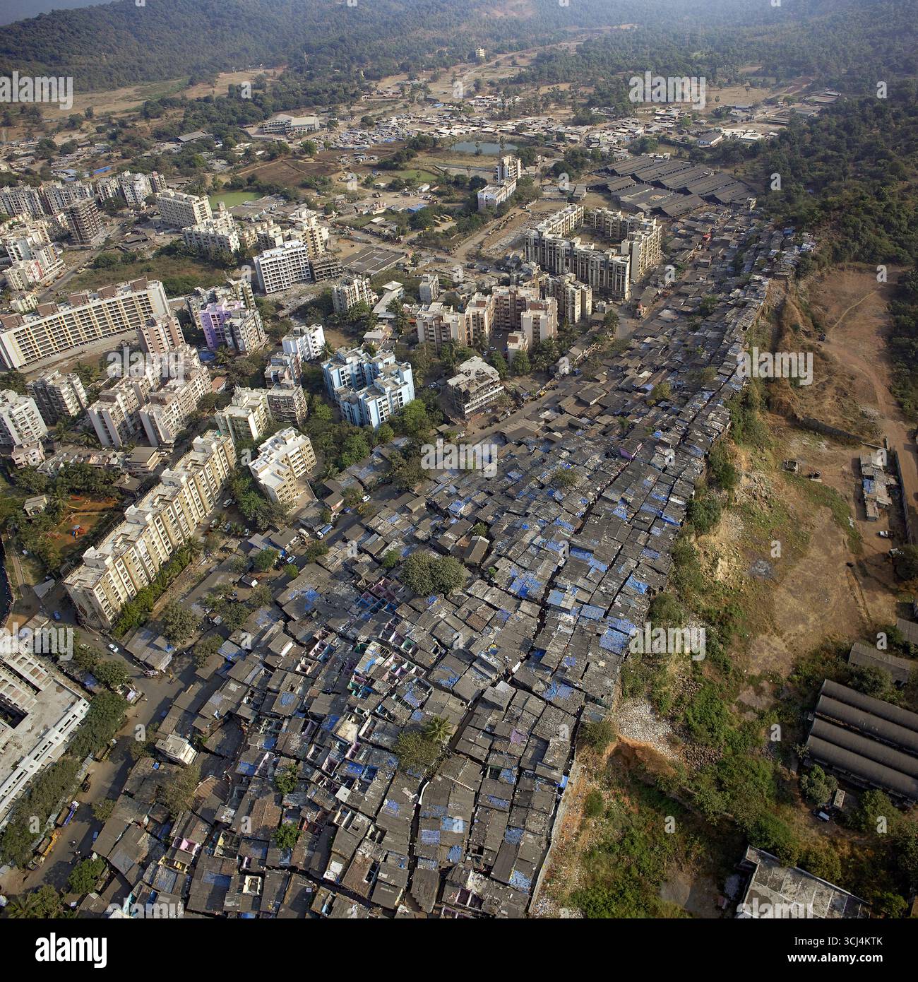Aerial view of dense, dark blue rooftops of a slum juxtaposed against ...