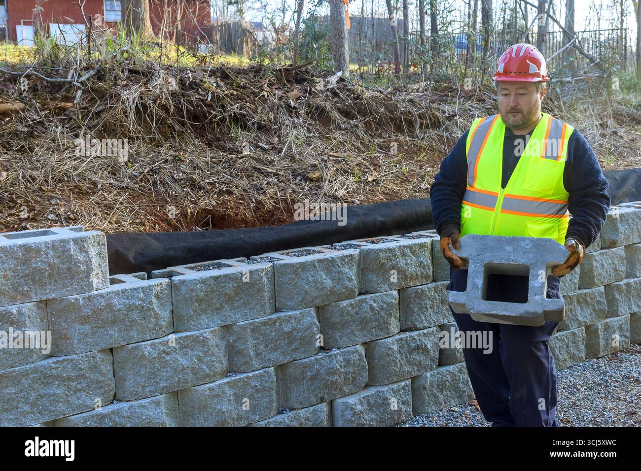 Construction worker in safety vest,helmet lifts block for retaining ...