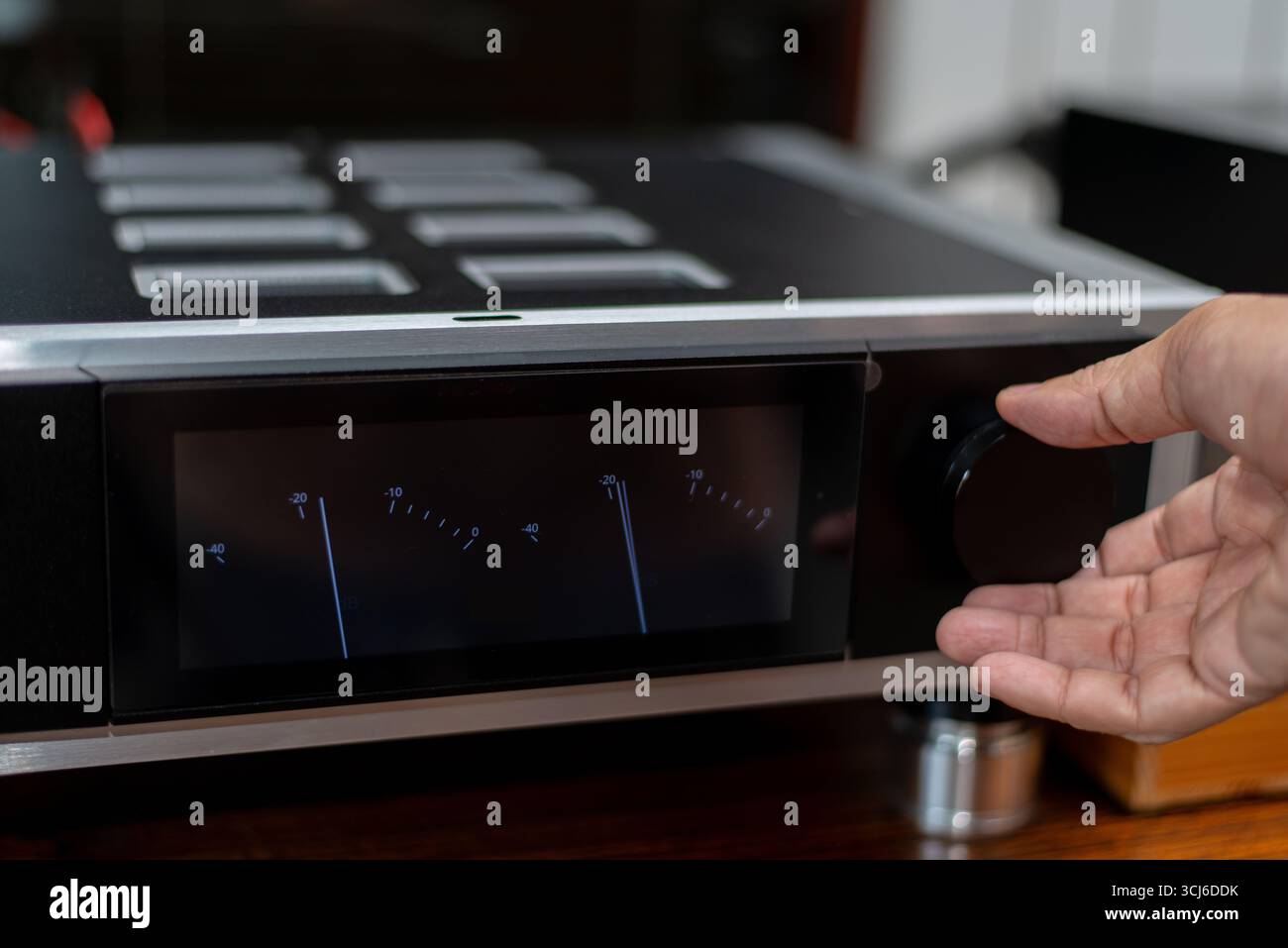 Close-up of a hand turning the volume knob on a modern Hi-Fi amplifier ...