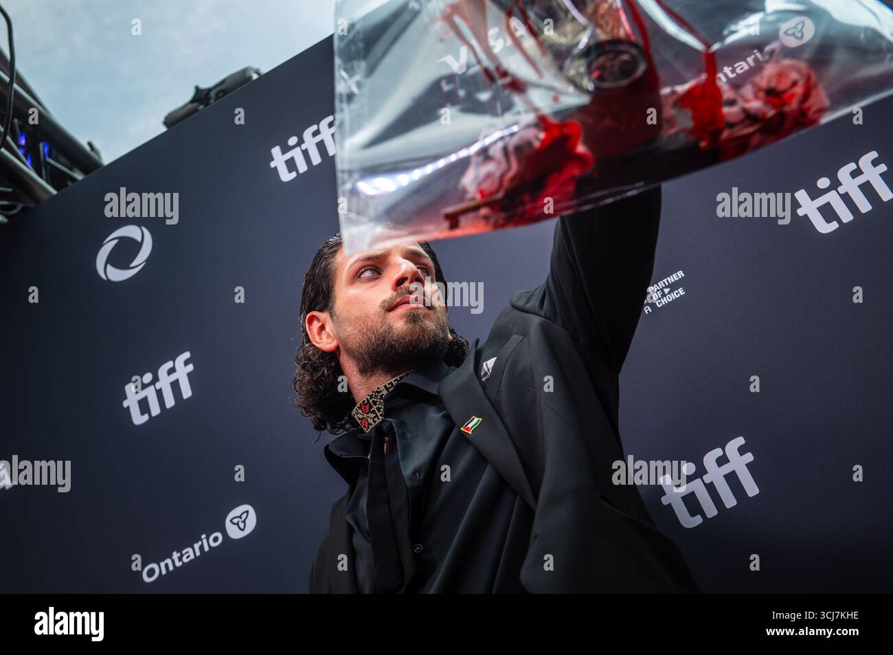 Karim Daoud Anaya holds up a camera soaked in fake blood on the red ...