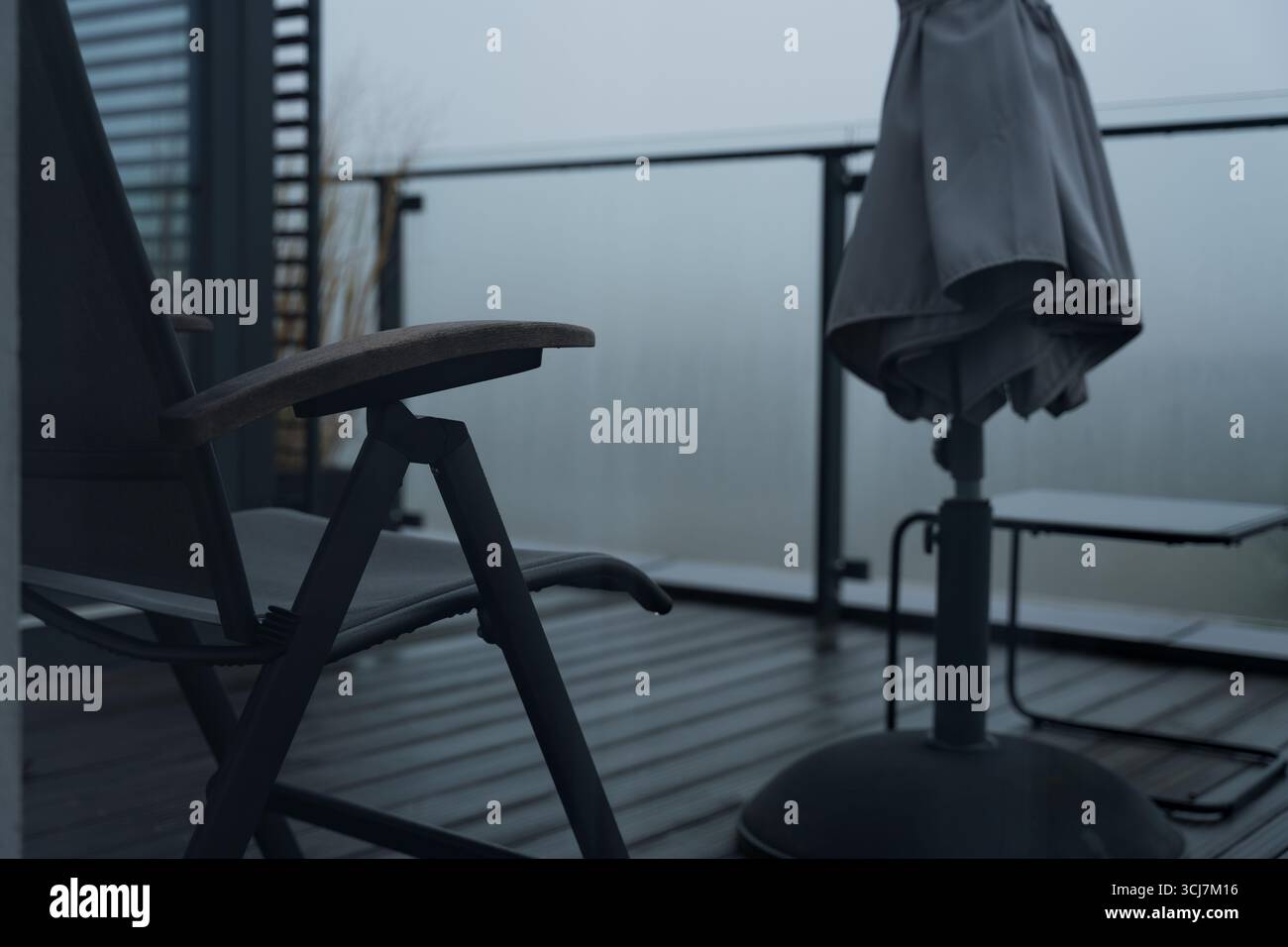 Autumn foggy balcony scene with closed umbrella, lounge chair, and ...