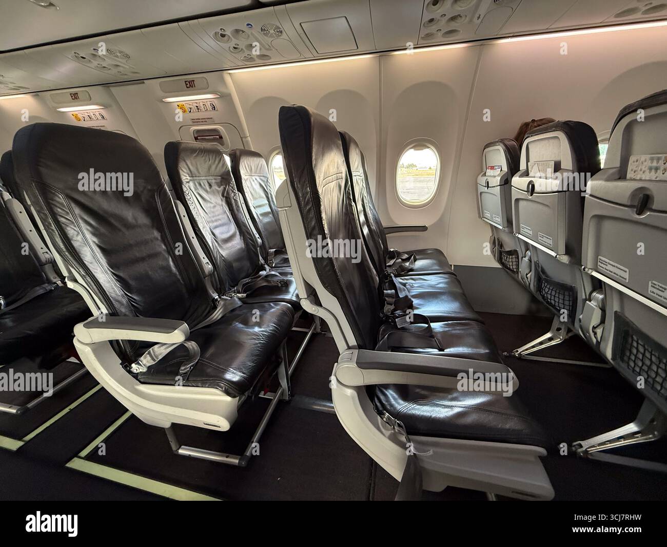 Empty black leather airplane seats next to a window with seatbelts ...
