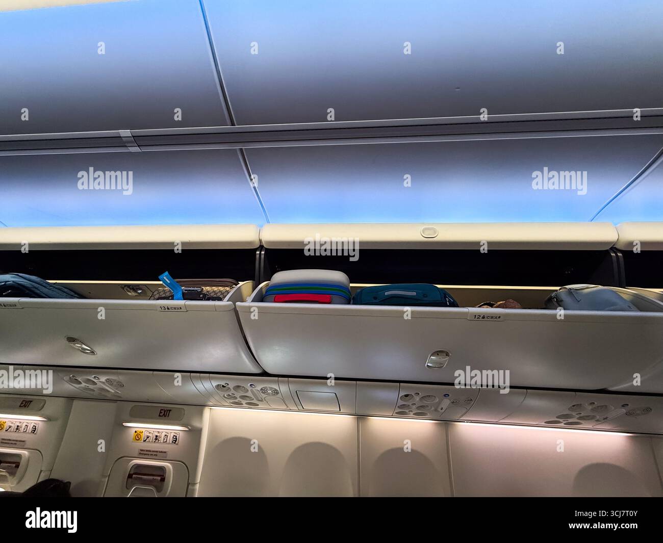 Overhead storage bins inside airplane cabin with luggage and personal ...