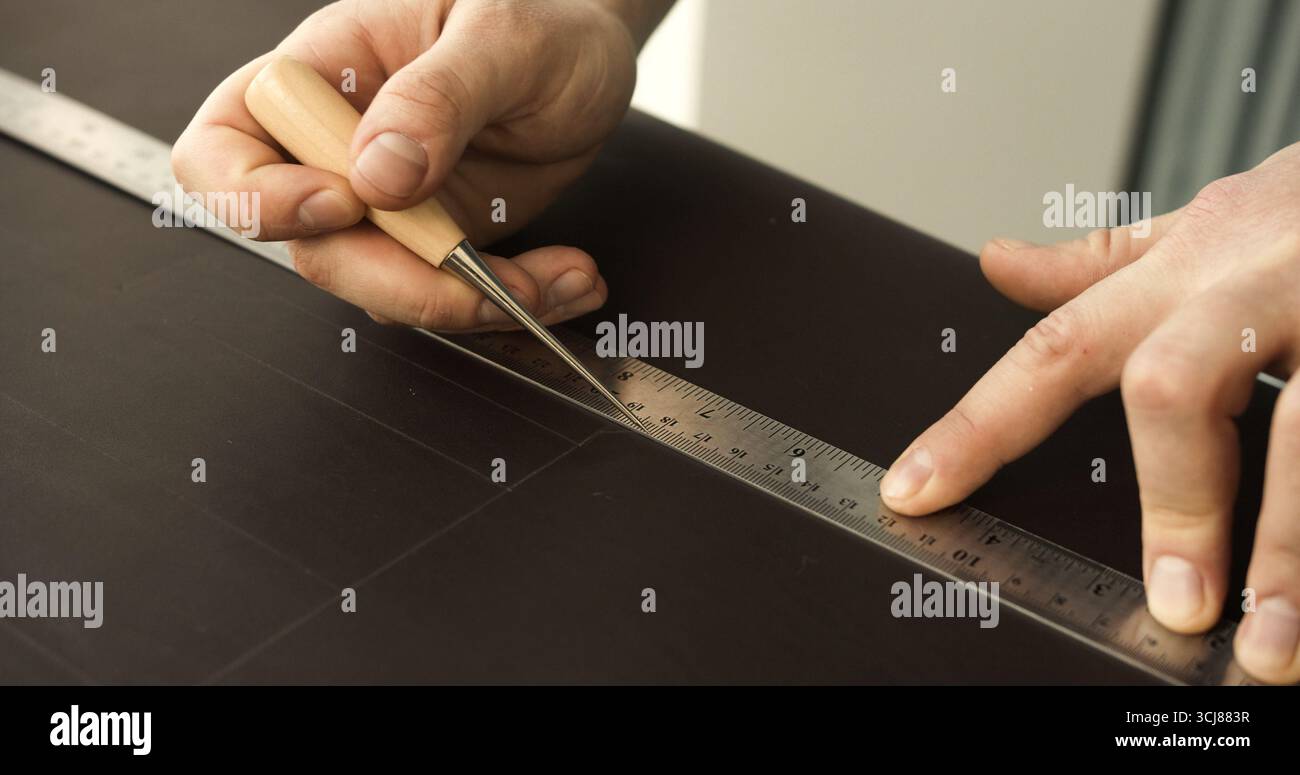 Hands of craftsman marking straight lines on leather sheet with awl and ...