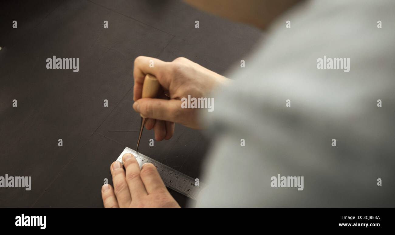 Craftsman using awl and ruler to mark layout lines on leather surface ...