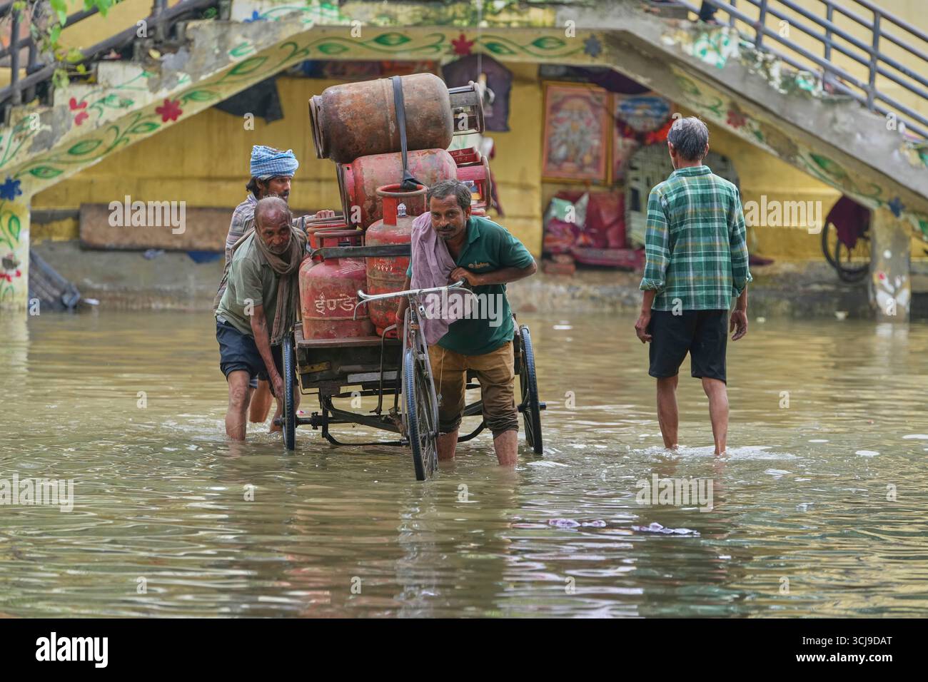 People help a rickshaw driver carrying gas cylinders to cross flooded ...