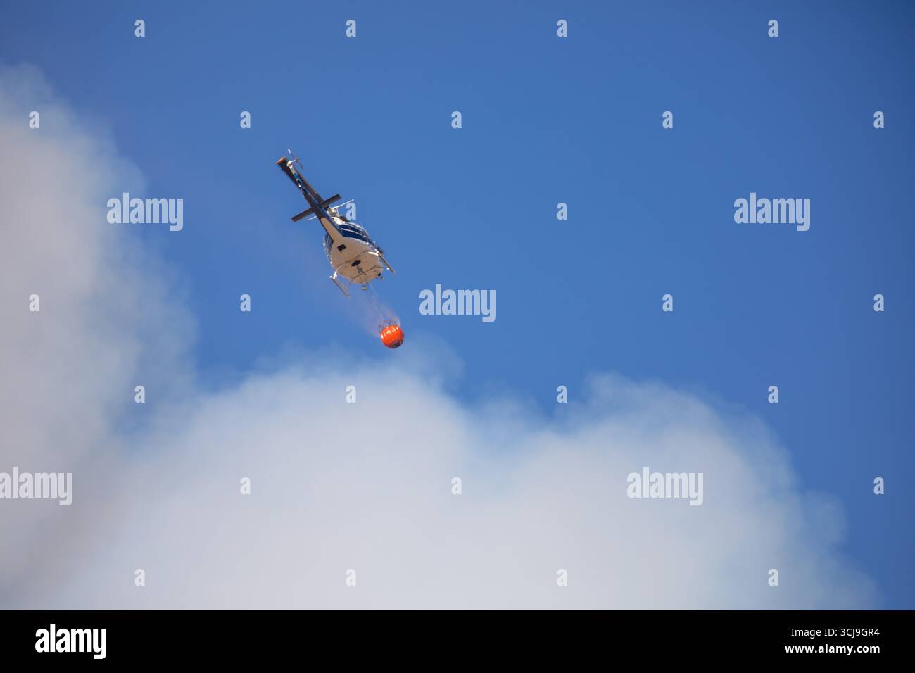 A helicopter is flying in the sky with a fire hose attached to it. The ...