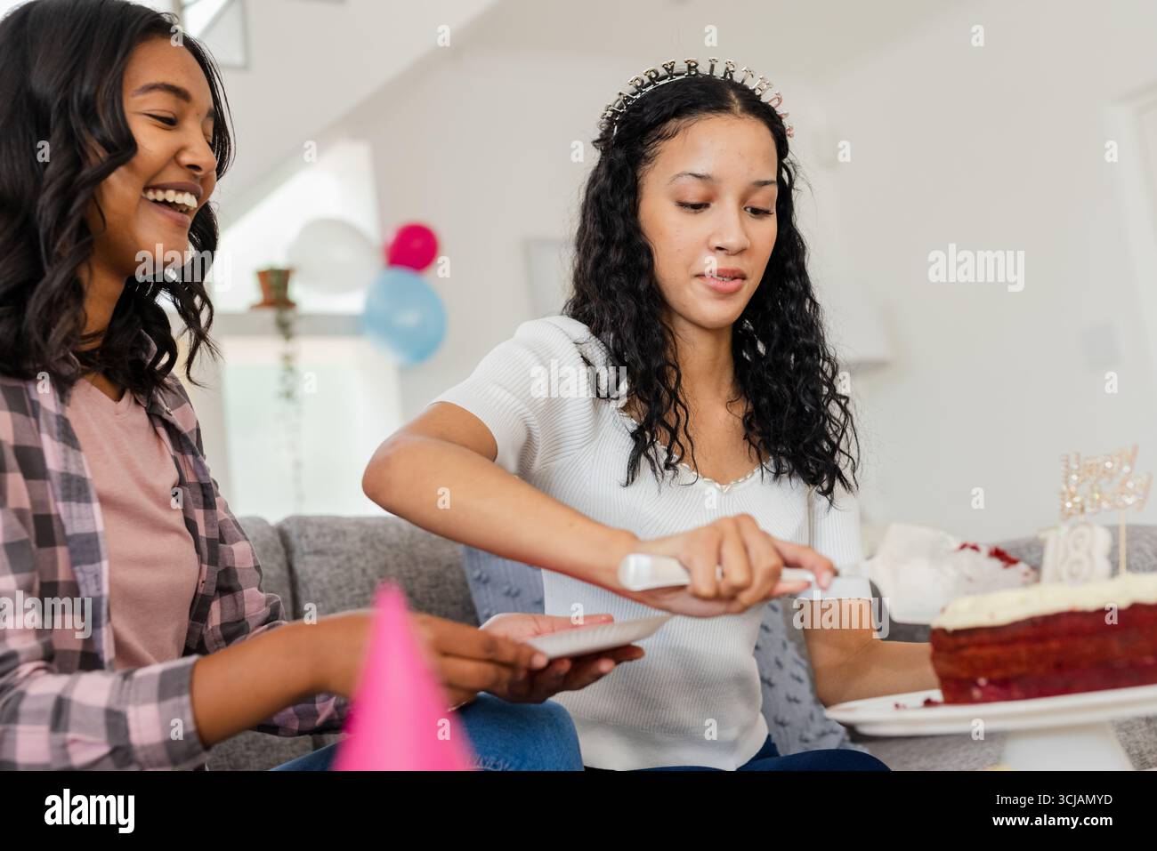 Celebrating birthday, young woman cutting cake while friend smiling on ...
