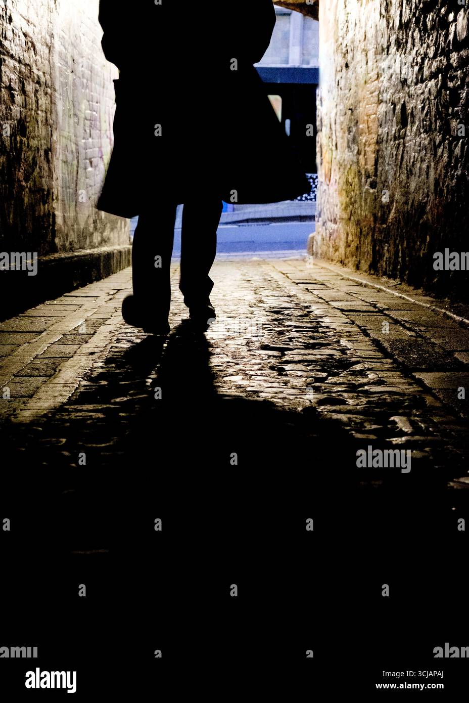 A person is walking down a narrow alleyway, their silhouette cast ...