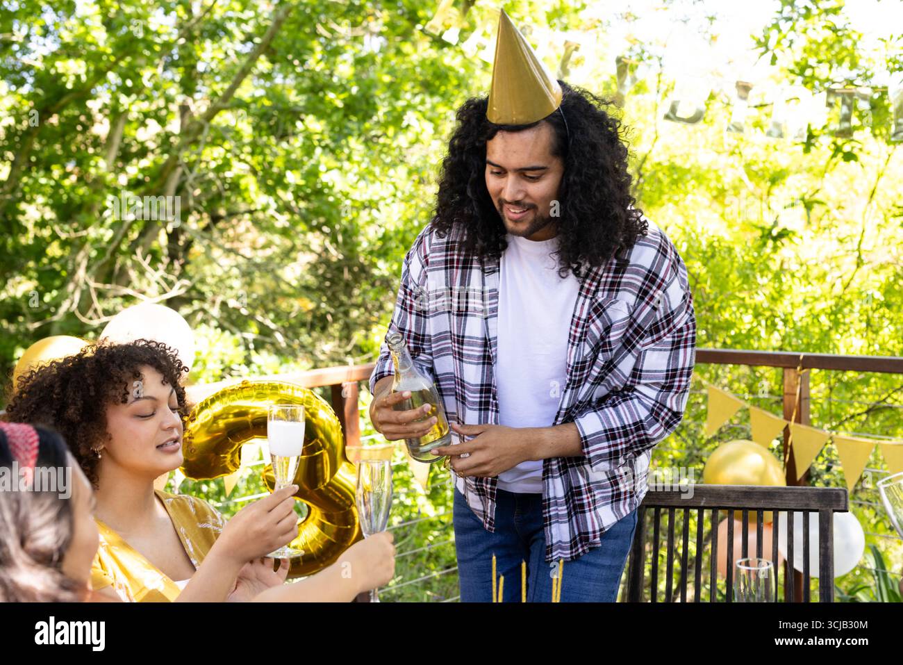 Man pouring champagne at outdoor birthday party with friends, wearing ...