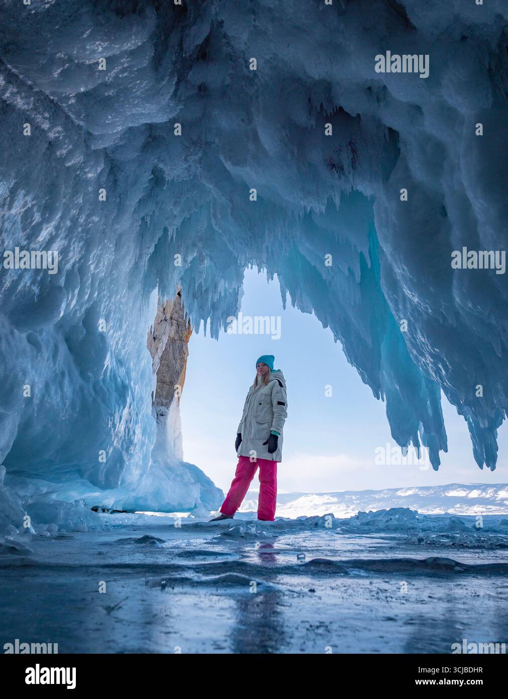 Young woman in winter gear stands inside a stunning ice cave on Baikal ...