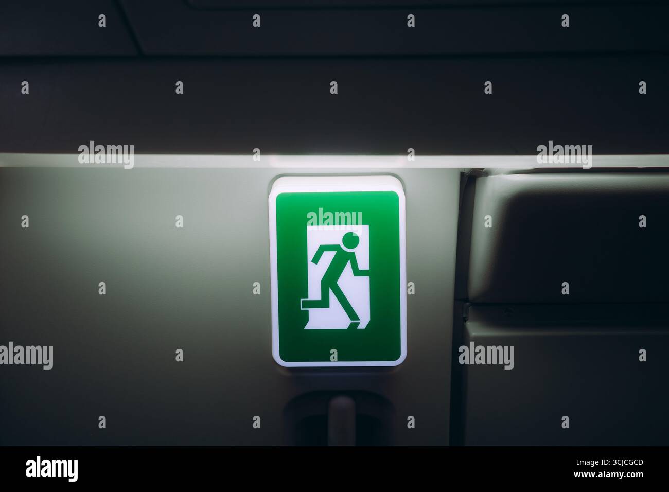 A bright green emergency exit sign is illuminated inside an aircraft ...