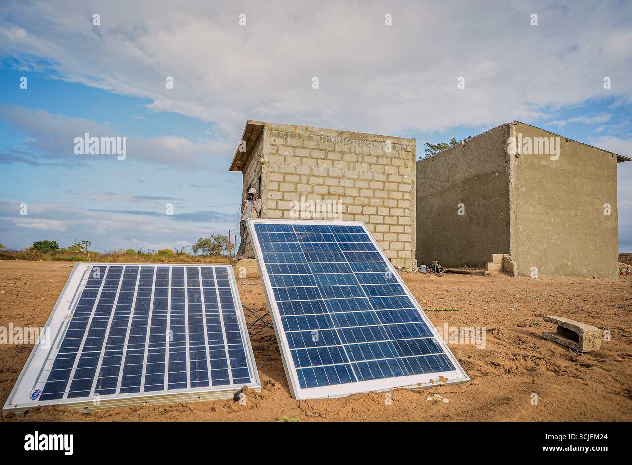 A man stands outside his home whilst using a mobile phone powered by solar panels, on the ...