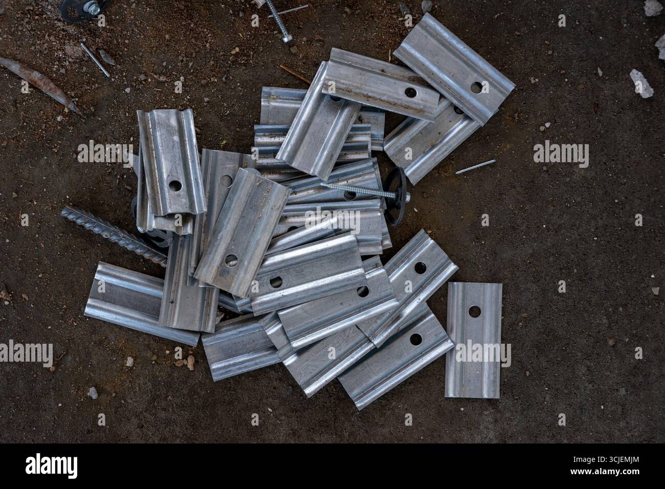 Stack of silver metal brackets with holes lying on rough soil ...