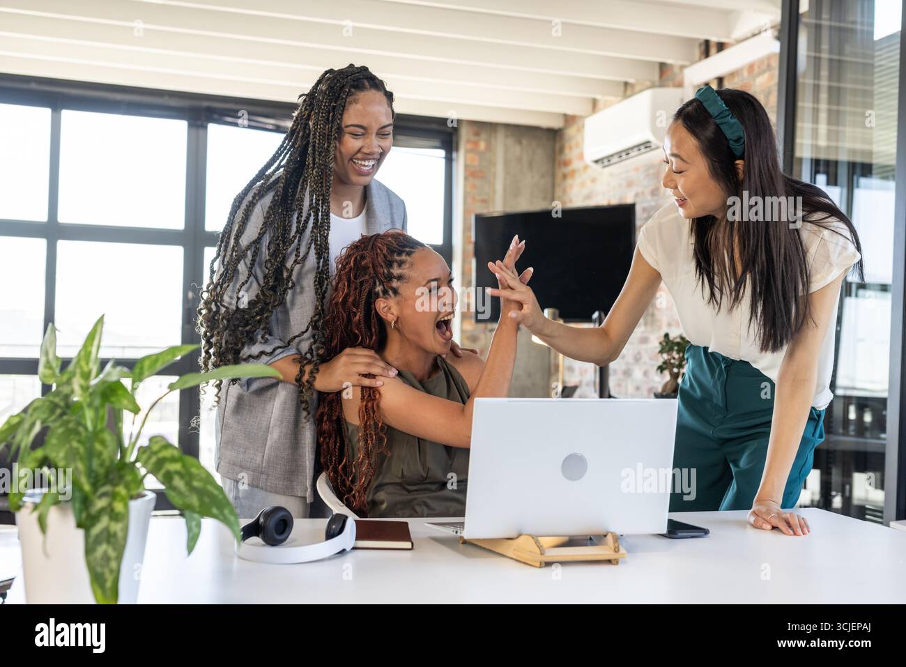 Celebrating success, diverse businesswomen high-fiving at office desk ...