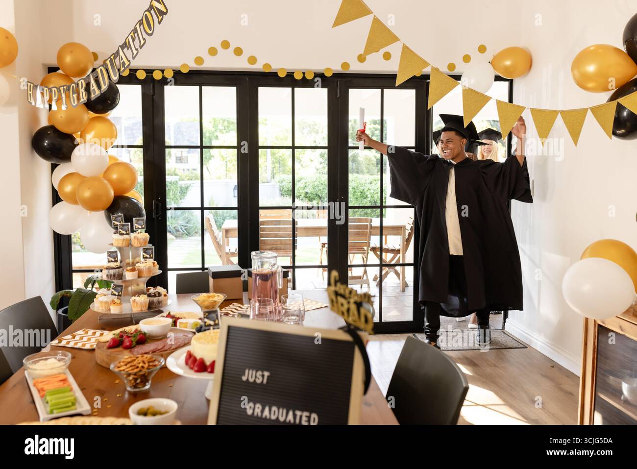 Graduate celebrating with friends at home, holding diploma and smiling ...