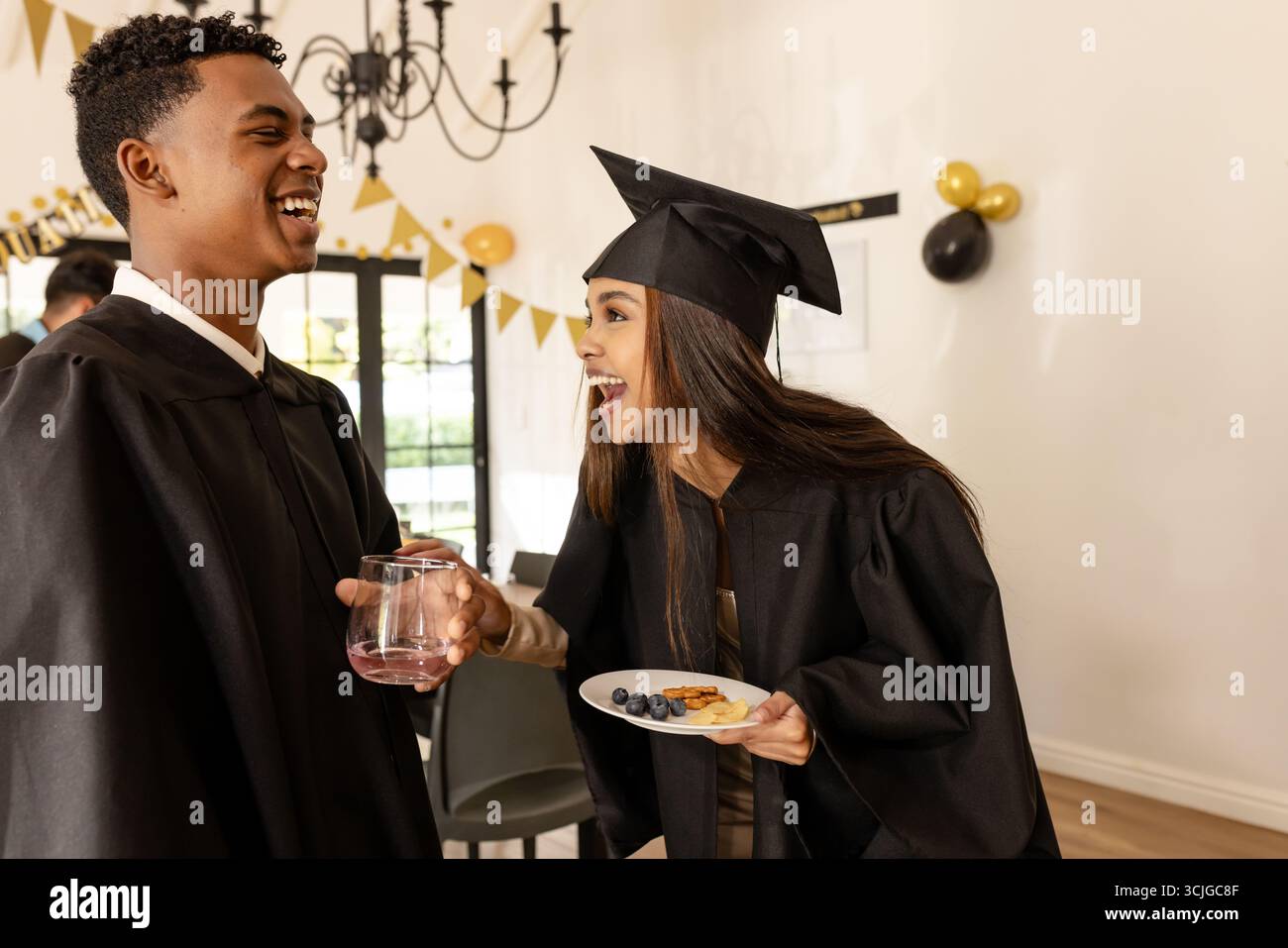 Graduates in caps and gowns celebrating with snacks and drinks at party ...