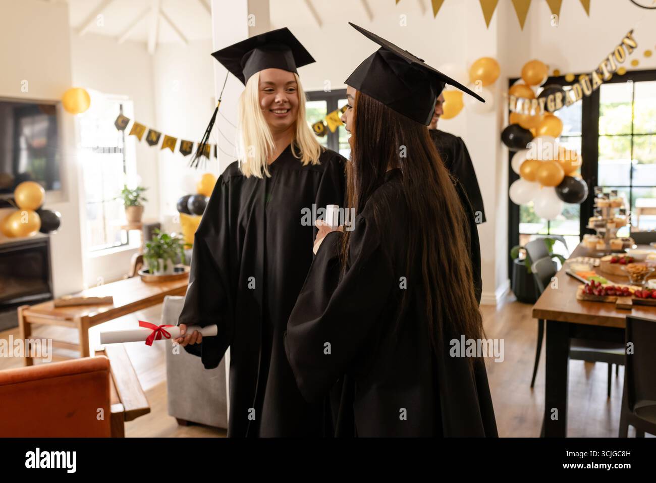 Graduates in caps and gowns celebrating at home with diplomas, smiling ...