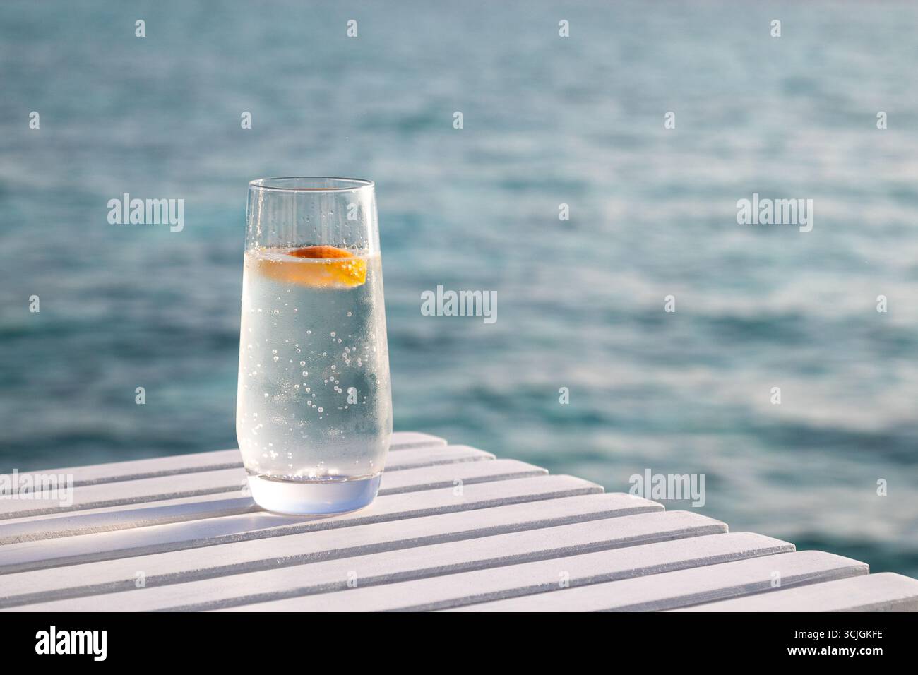 Glass of chilled water with citrus, left of frame, on a white table ...