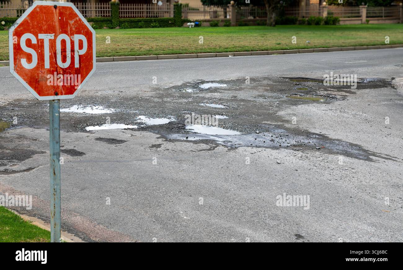 Old looking stop sign on the left and water filled potholes in a ...
