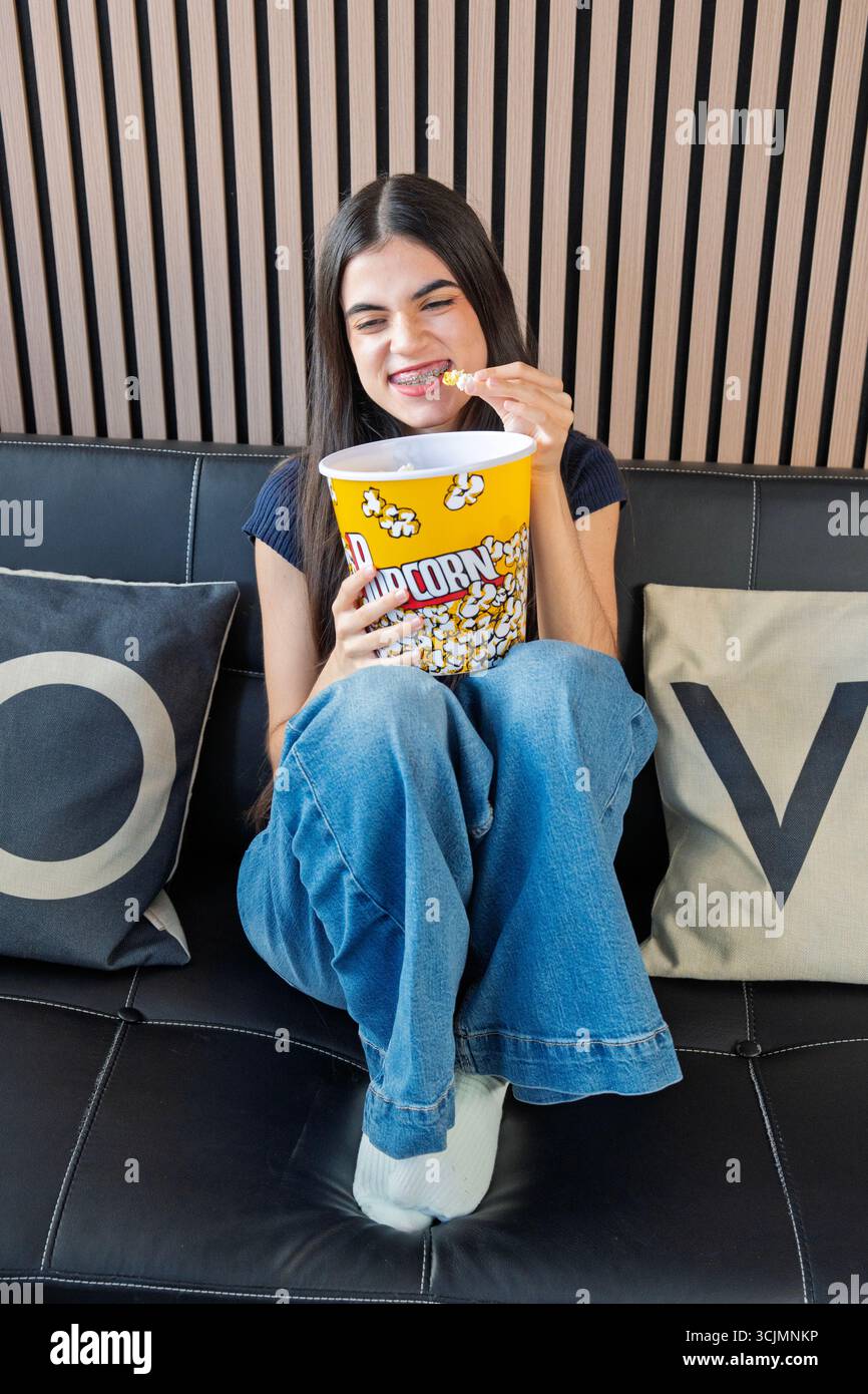 Teenager eating popcorn from a big bucket while sitting on a ...